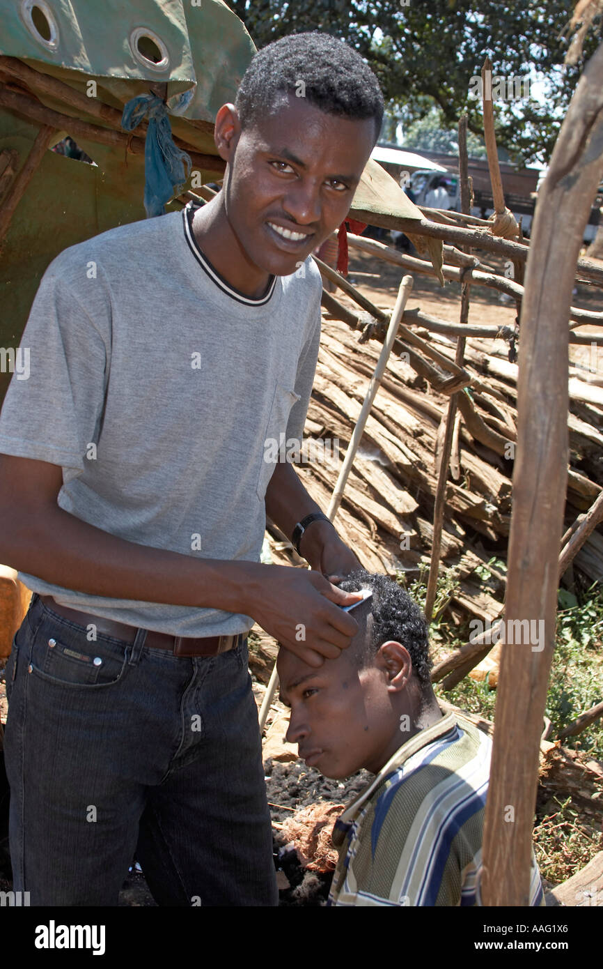 Barber man cutting hair with a comb and razor on market day in village ...