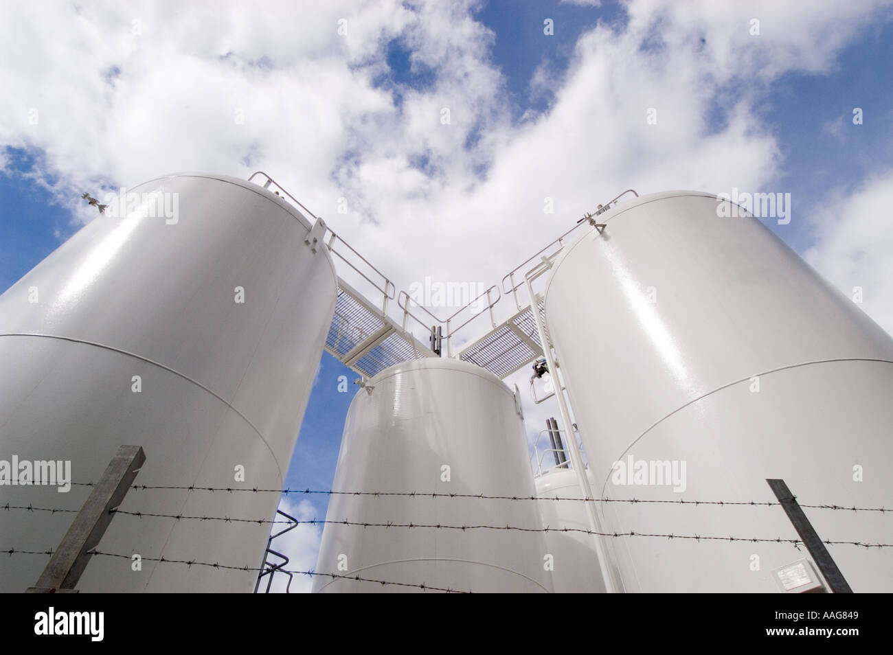 Storage Tanks behind a fence seen against a blue sky with clouds Stock ...