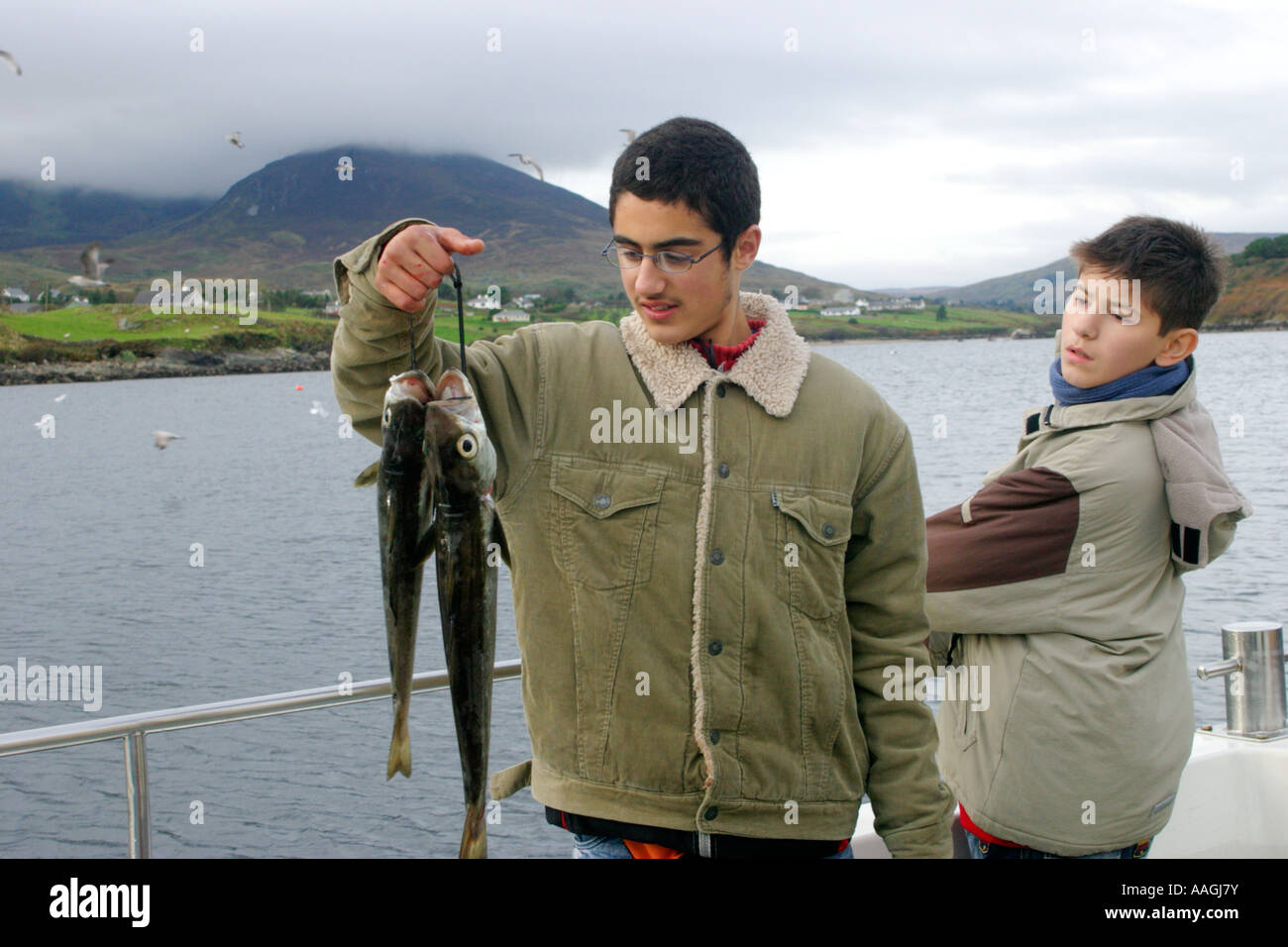 young boy with two fish he has caught in the Atlantic Ocean in County ...