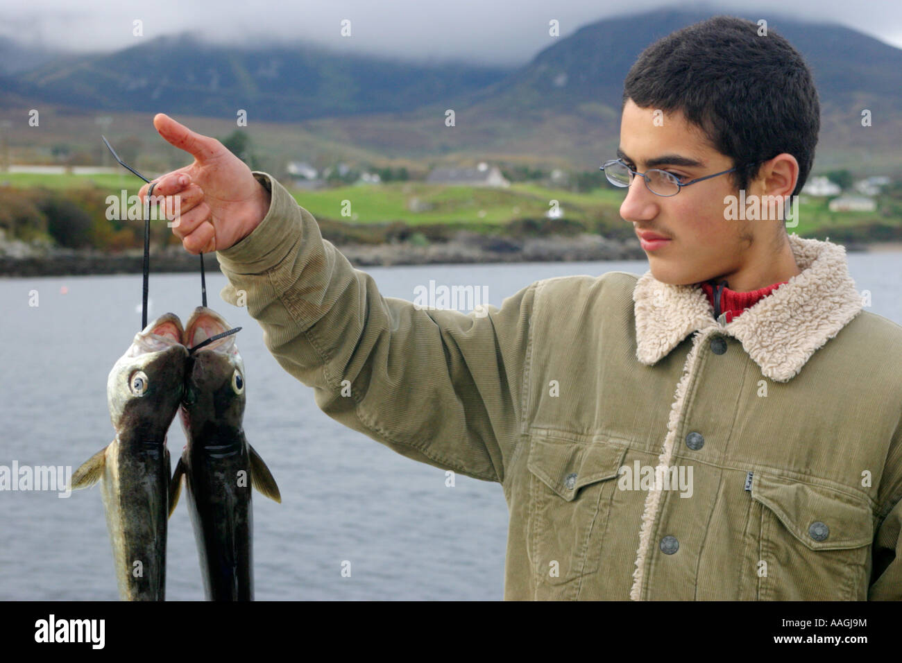 young boy with two fish he has caught in the Atlantic Ocean in County ...