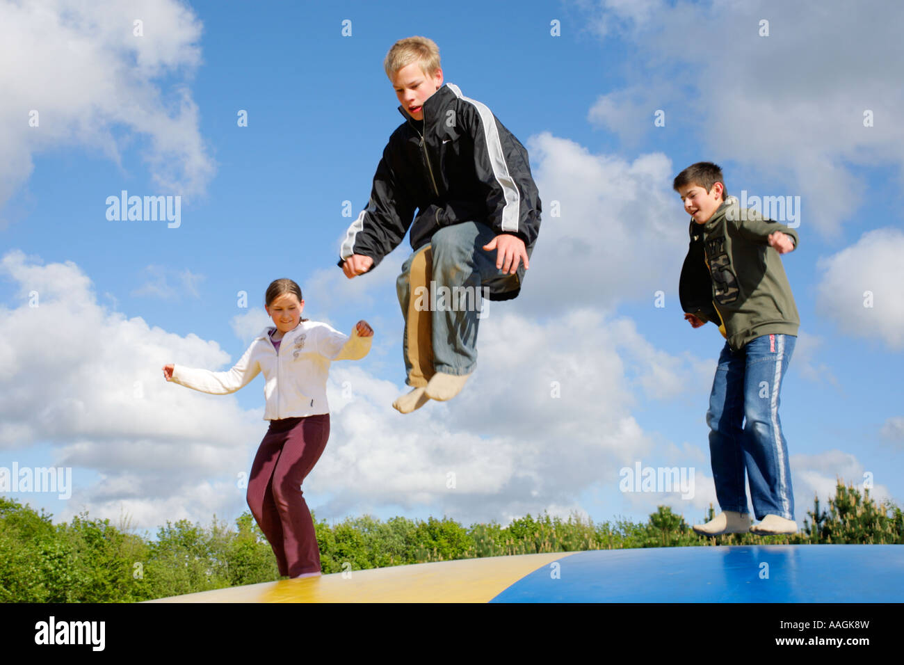 three kids jumping on a big rubber trampoline Stock Photo - Alamy