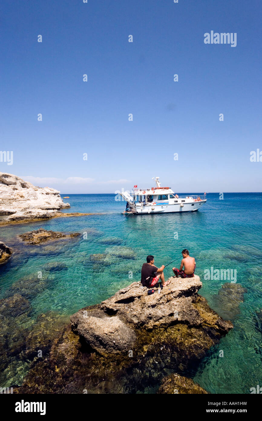 Two men fishing on a rock near Thermae Kallithea ship passing Rhodes ...