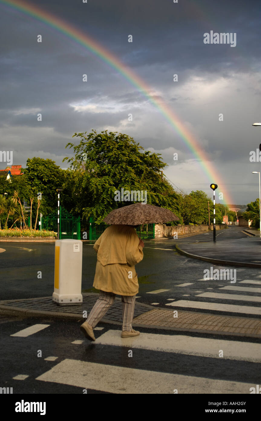 Woman walking across zebra crossing with umbrella and rainbow in the ...