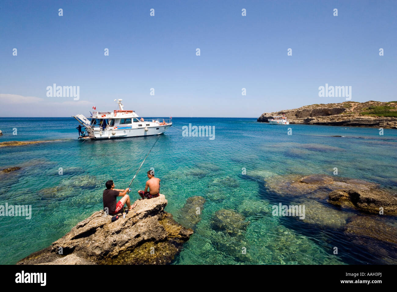 Two men fishing on a rock near Thermae Kallithea ship passing Rhodes ...