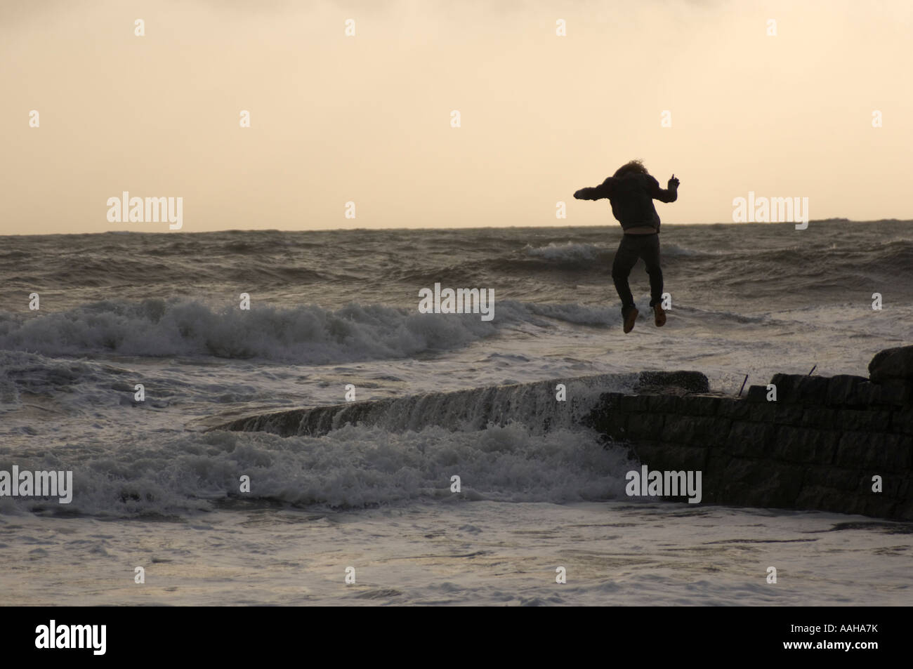 young man jumping on stone jetty during a storm dodging the waves ...