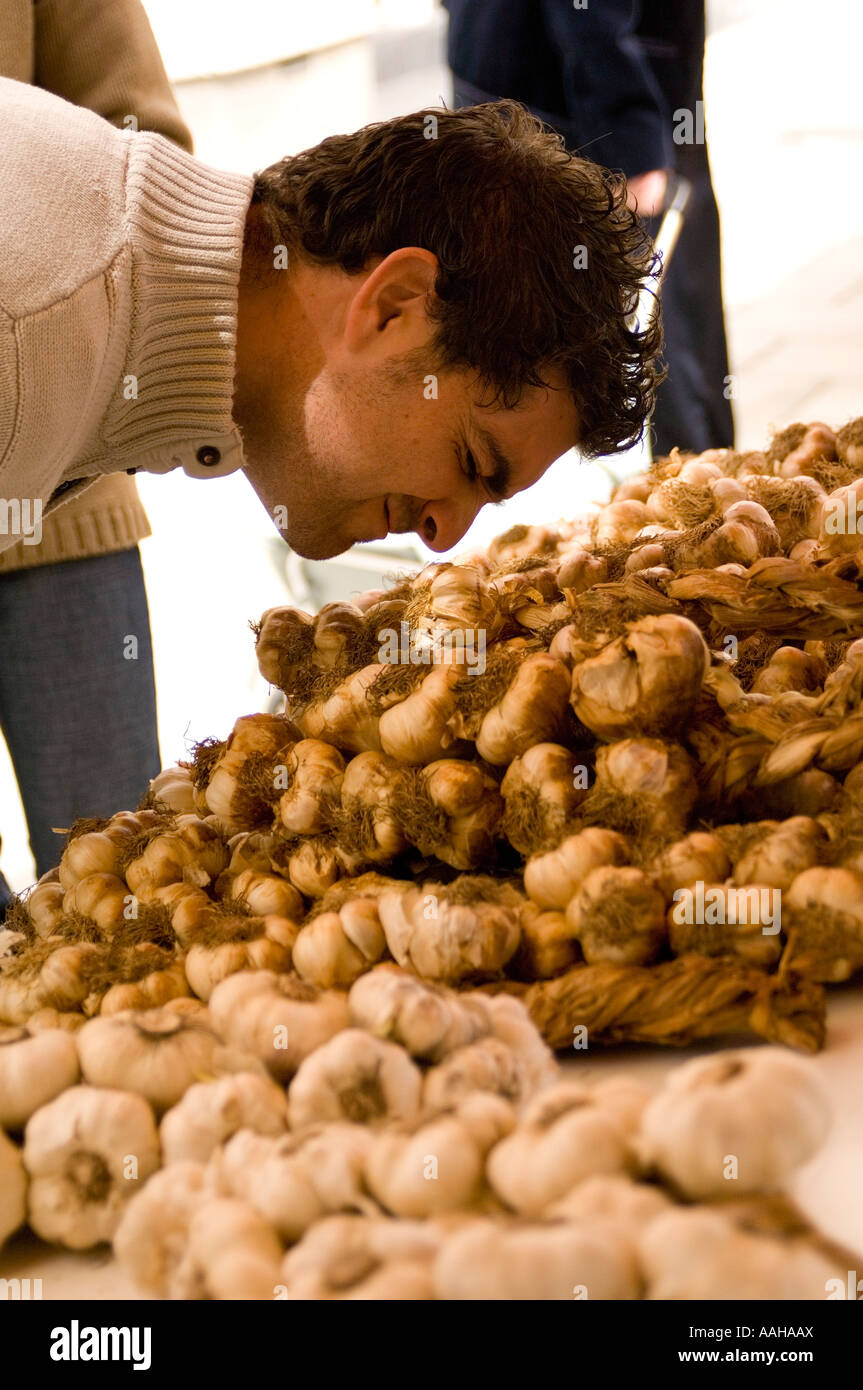 man smelling bunches of smoked french garlic bulbs on a market stall ...