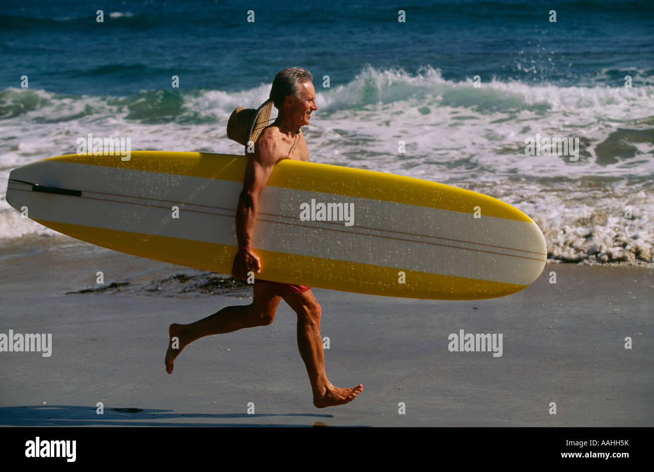 Senior man with surfboard running on beach Stock Photo - Alamy