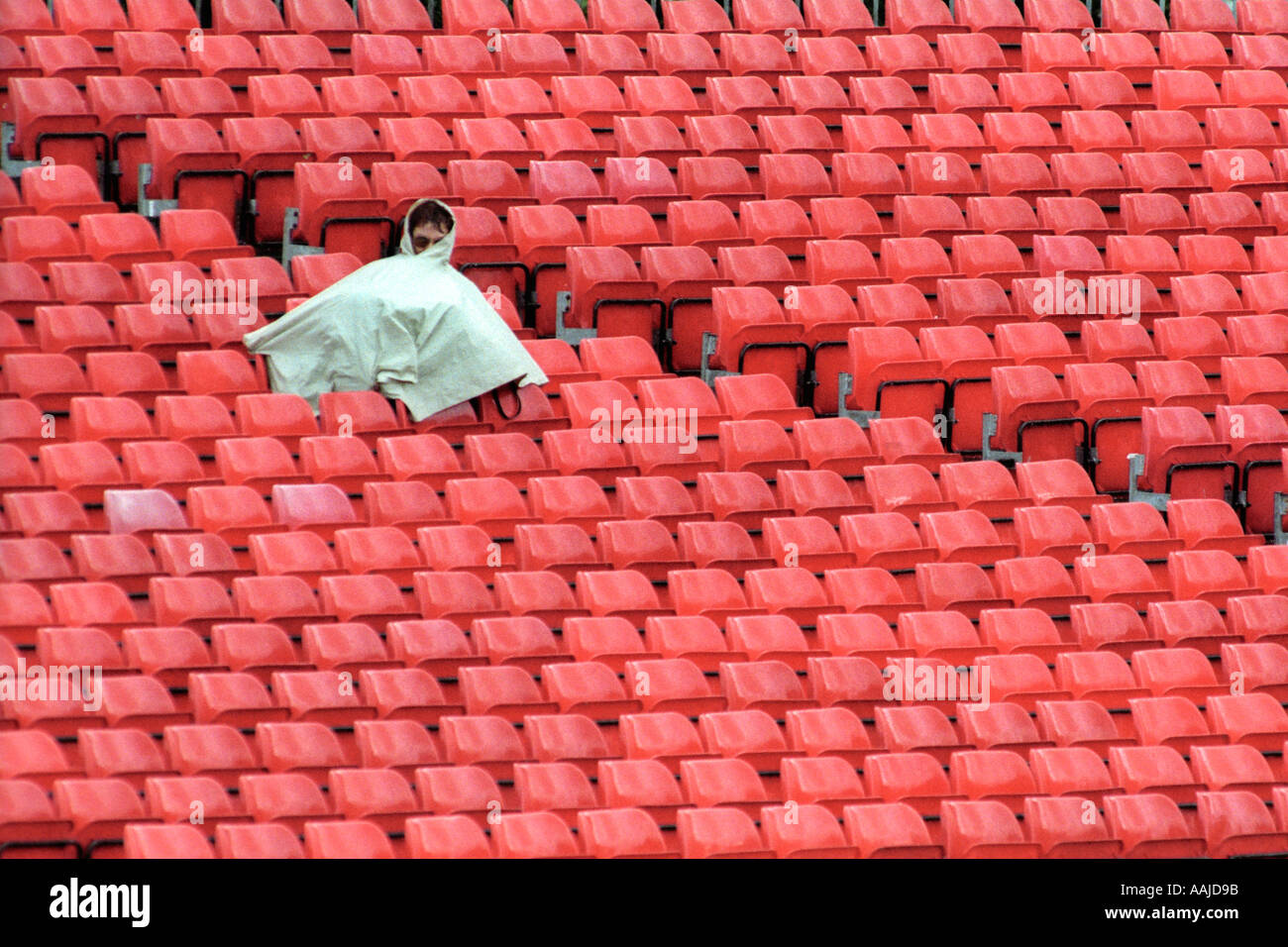 Fan taking shelter at a rain sodden cricket match while waiting for ...