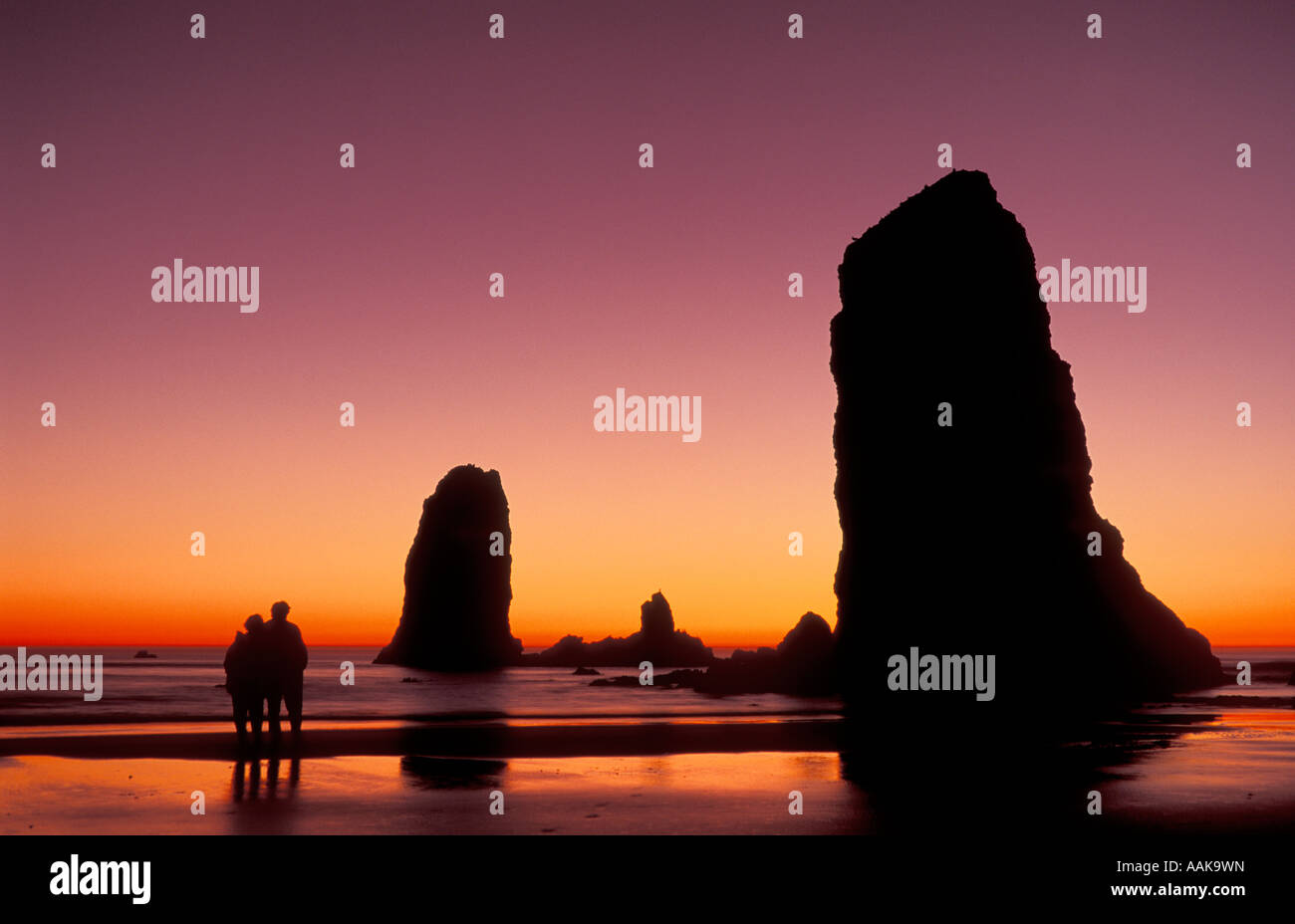 Haystack Rock sea stacks at sunset with couple on beach Cannon Beach ...