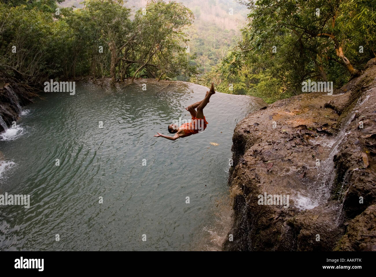 Novice monk doing a back flip of the rocks in a pool beneath the upper ...