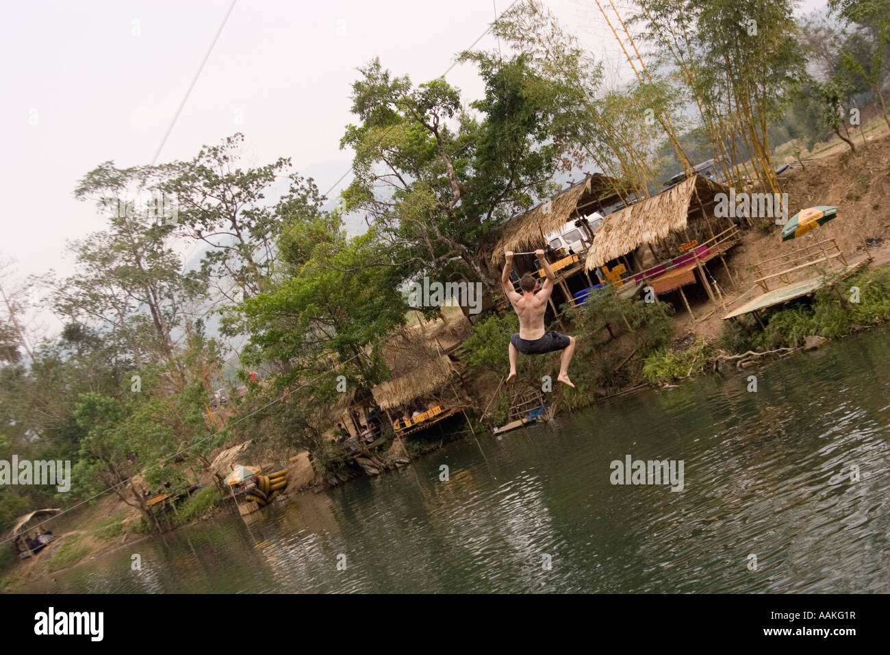 Tourist swings on rope swing while tubing down the Nam Xong river Vang ...
