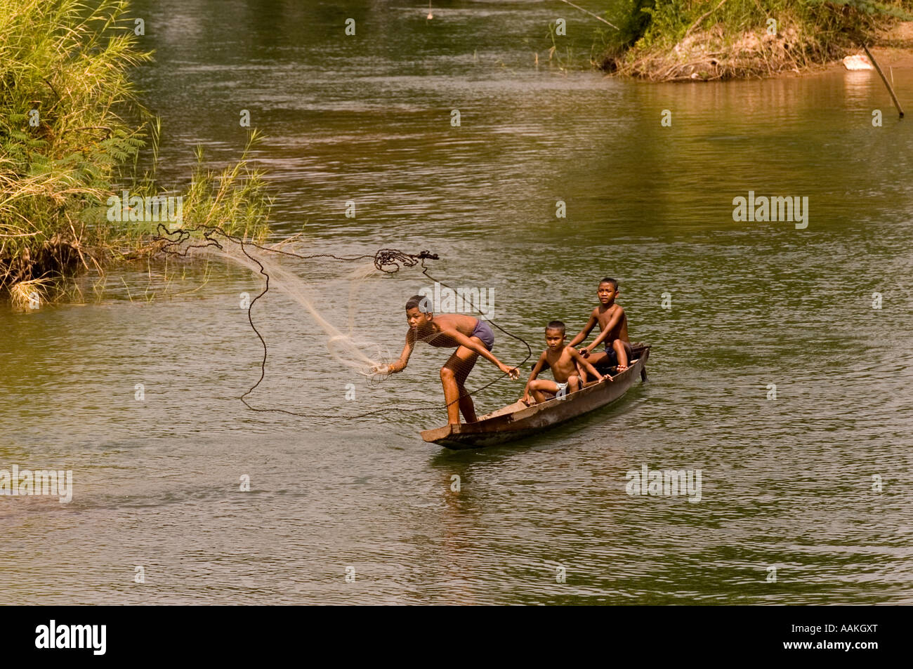 Boy throwing fishing net from boat in the Mekong river Don Det Laos ...