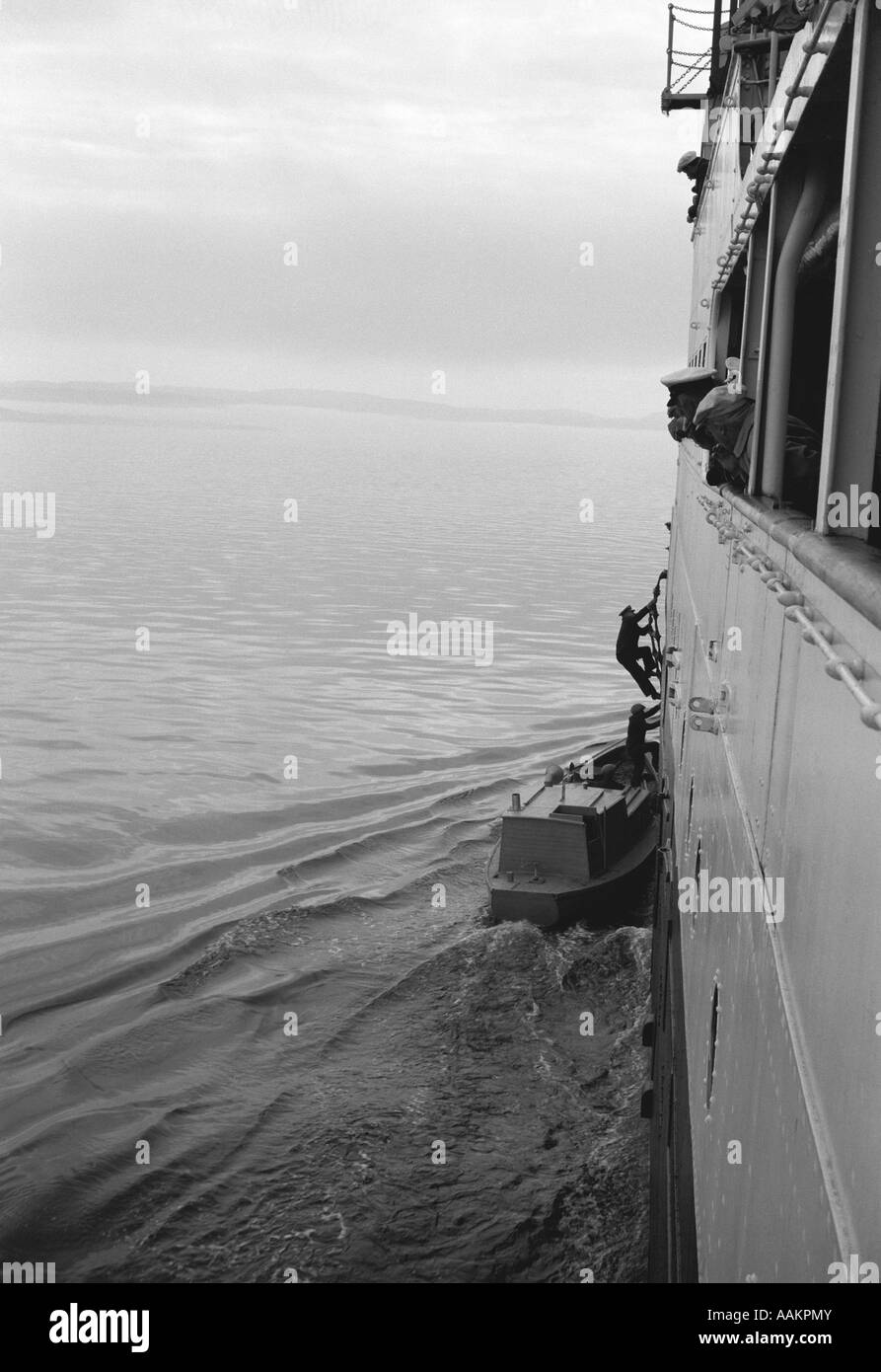 1950s MAN CLIMBING ABOARD SHIP FROM SMALL MOTOR LAUNCH UP A ROPE LADDER ...