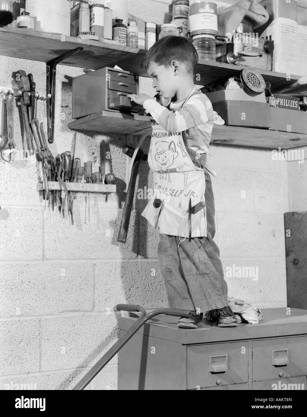1950s 4 YEAR OLD BOY IN GARAGE TOOL SHED STANDING ON CABINET TO REACH ...