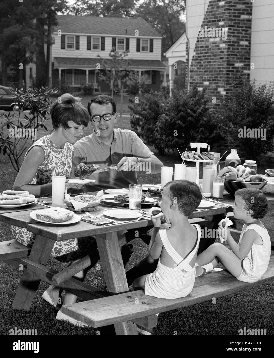 1960s SUBURBAN FAMILY OF FOUR AT PICNIC TABLE IN BACKYARD EATING Stock ...