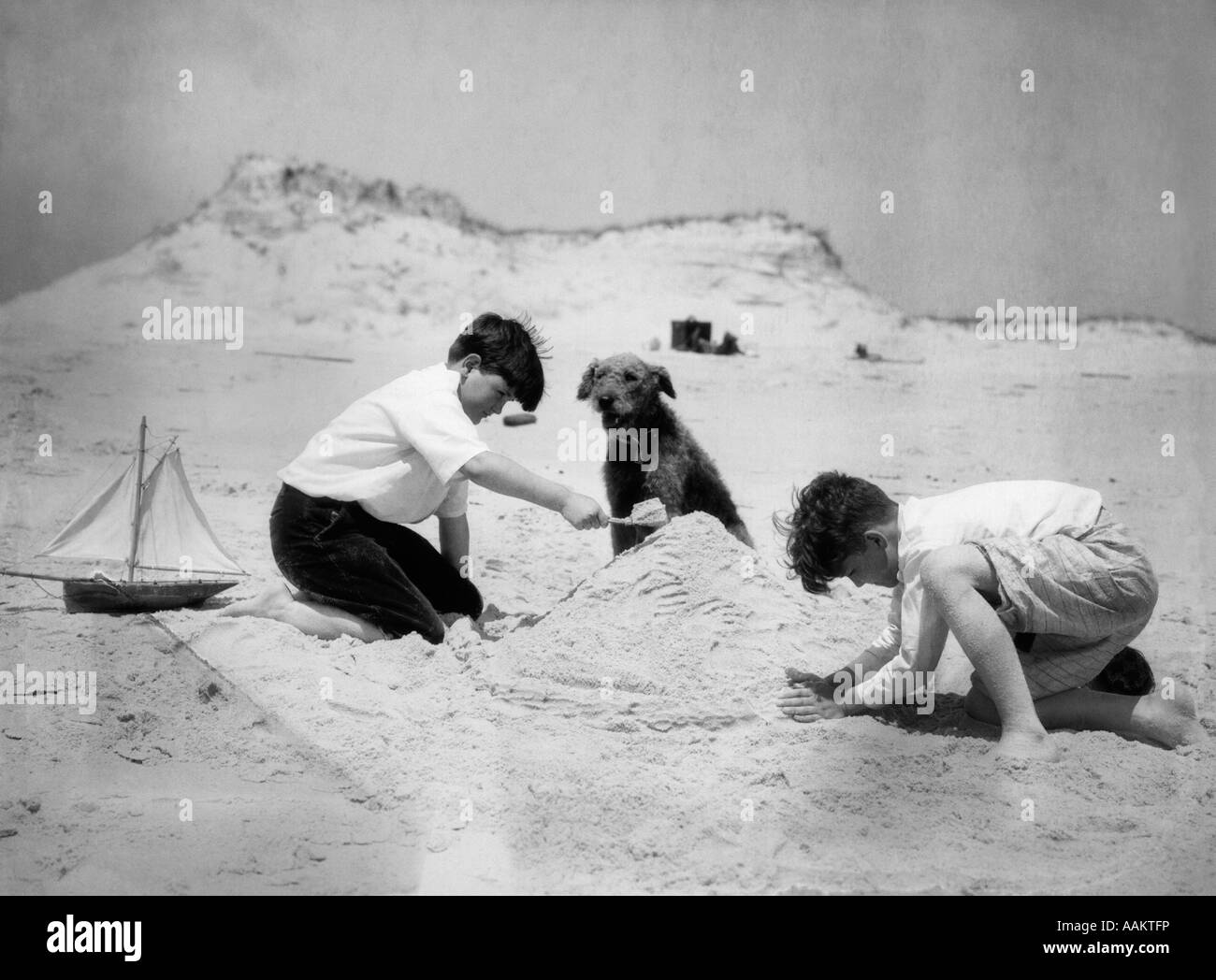 1920s 1930s TWO BOYS AND DOG PLAYING ON BEACH DIGGING MAKING SAND PILE ...