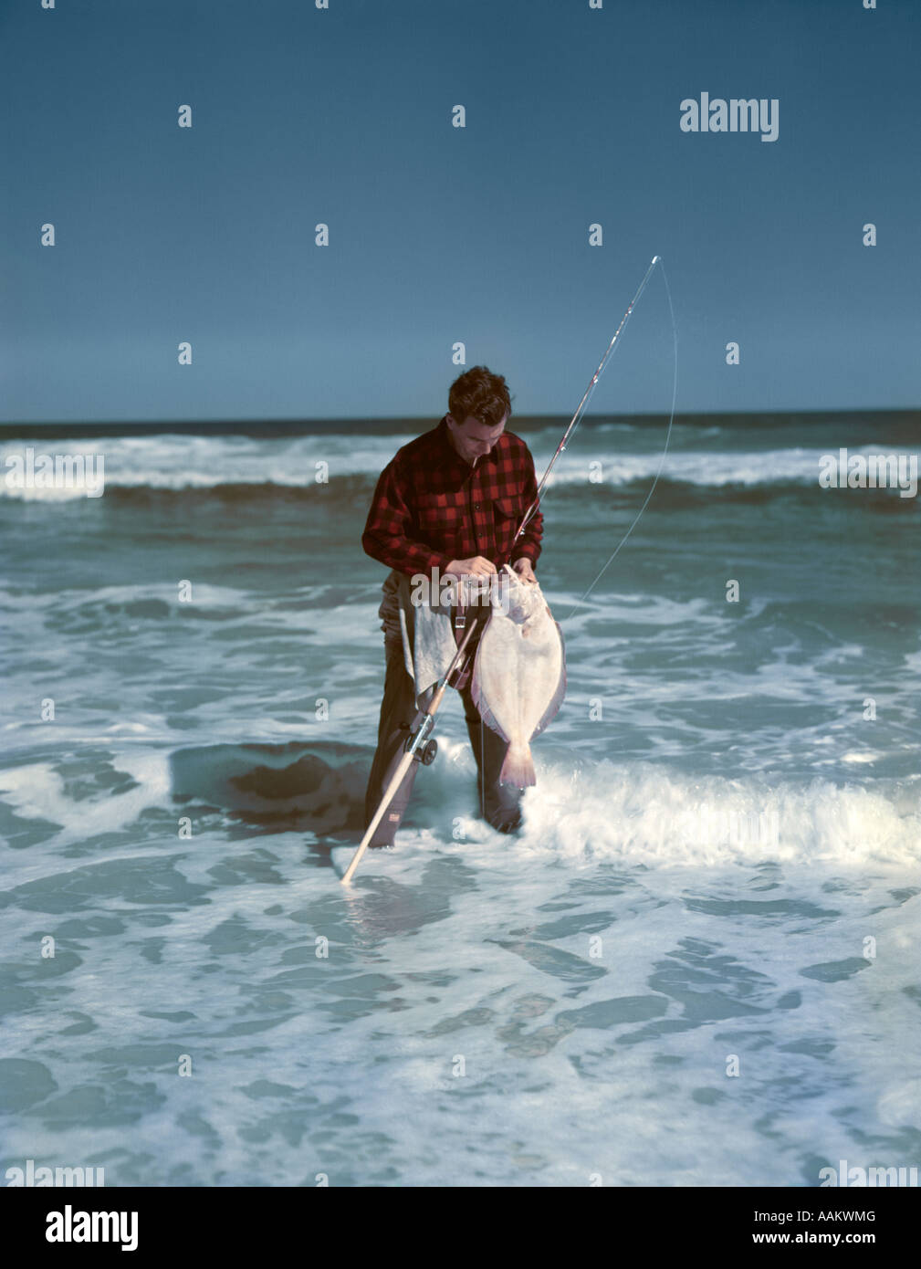 1950s MAN RED BLACK CHECKED SHIRT STAND IN SURF REMOVING FLOUNDER FROM ...