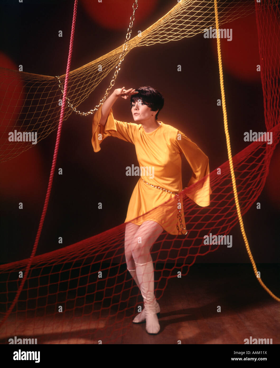 1960s 1970s YOUNG WOMAN IN SHORT GOLD TUNIC DRESS DANCING AMONG NETS ...