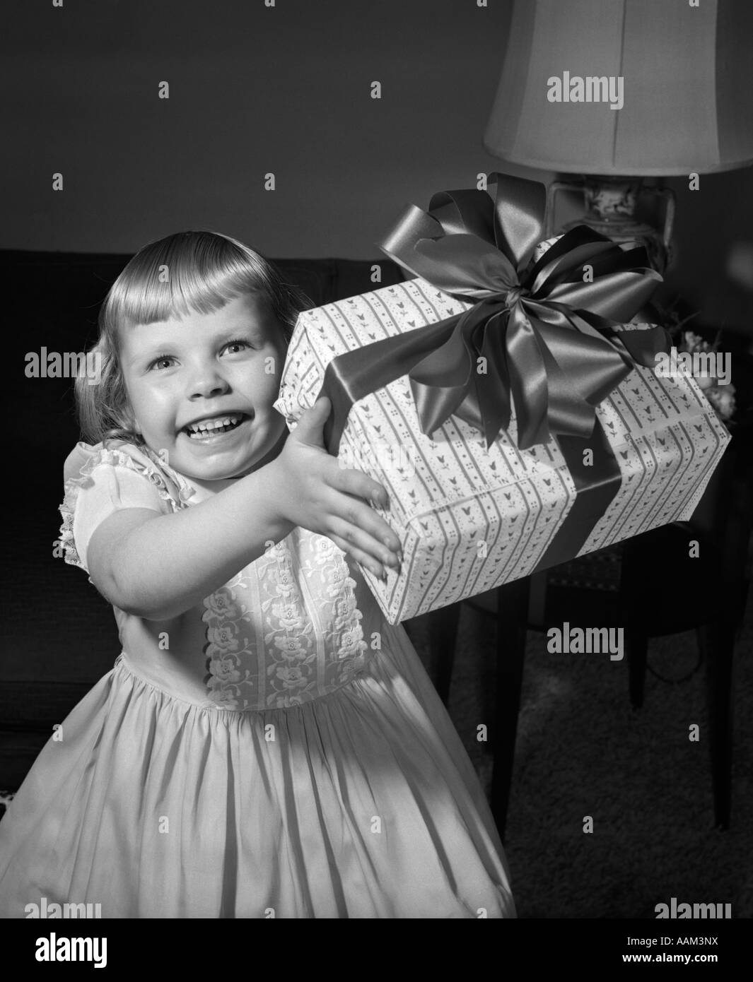 1950s SMILING GIRL HOLDING UP GIFT WRAPPED PRESENT Stock Photo - Alamy