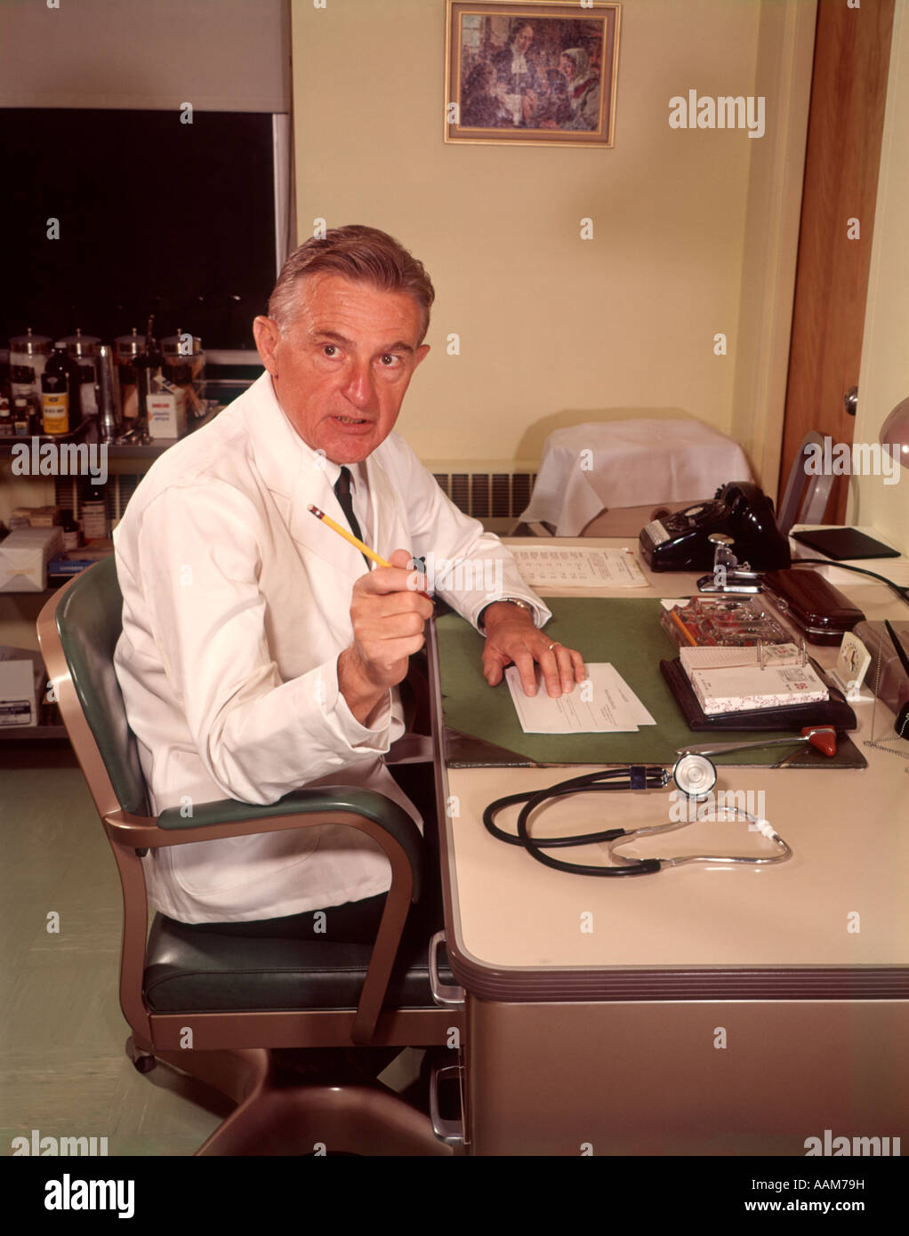 1960s DOCTOR POINTING WITH PENCIL SEATED AT DESK IN OFFICE DOCTORS ...