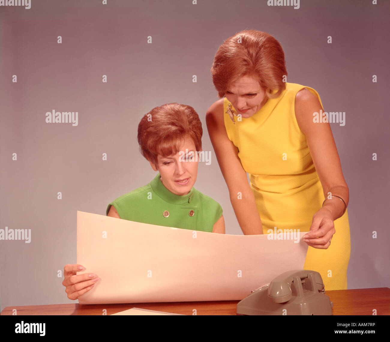 1960s TWO WOMEN EXECUTIVES AT DESK WITH TELEPHONE LOOKING AT WORKSHEET ...