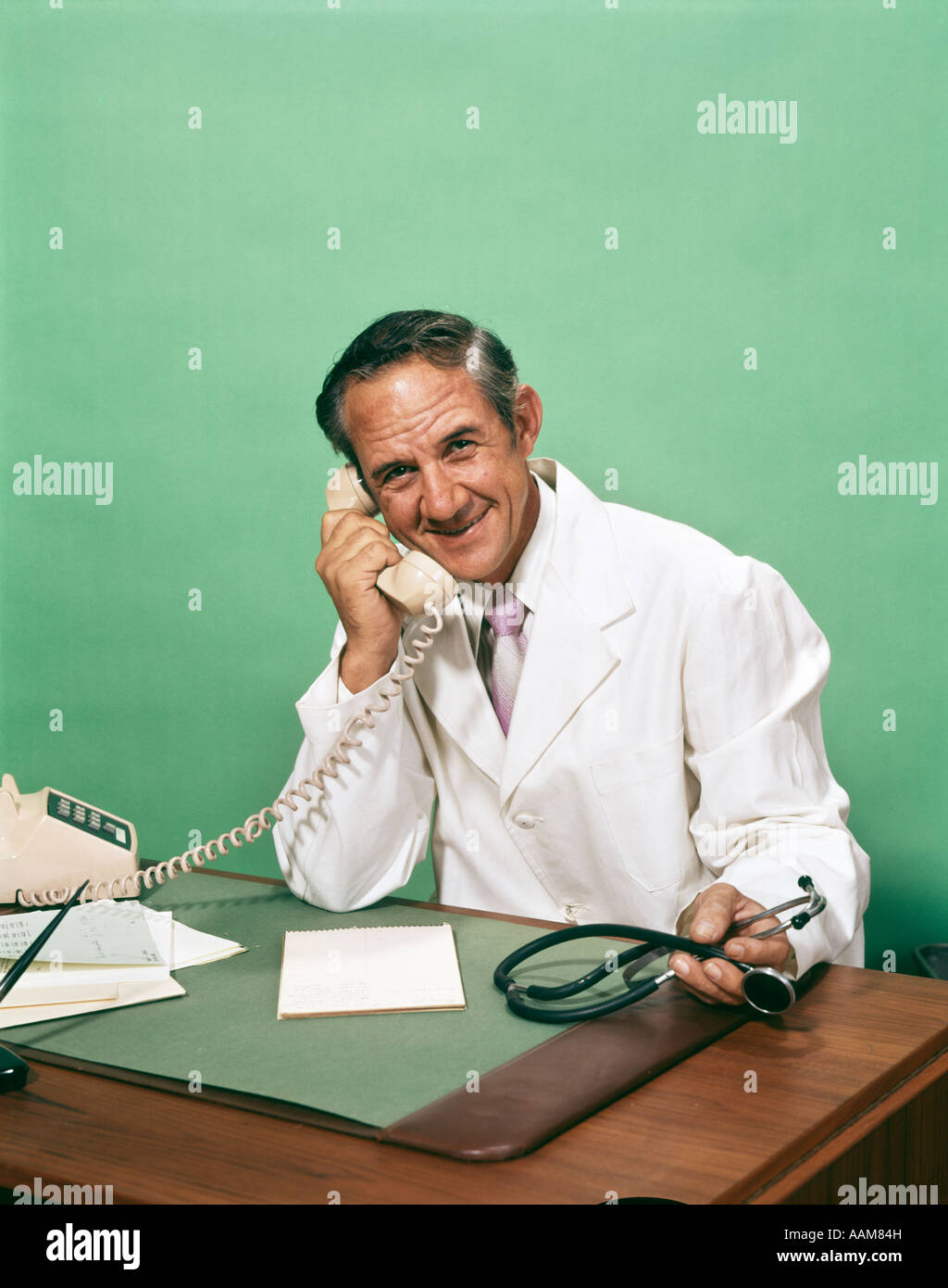 1970s PORTRAIT DOCTOR PHYSICIAN DESK TALKING TELEPHONE SMILING HOLD ...