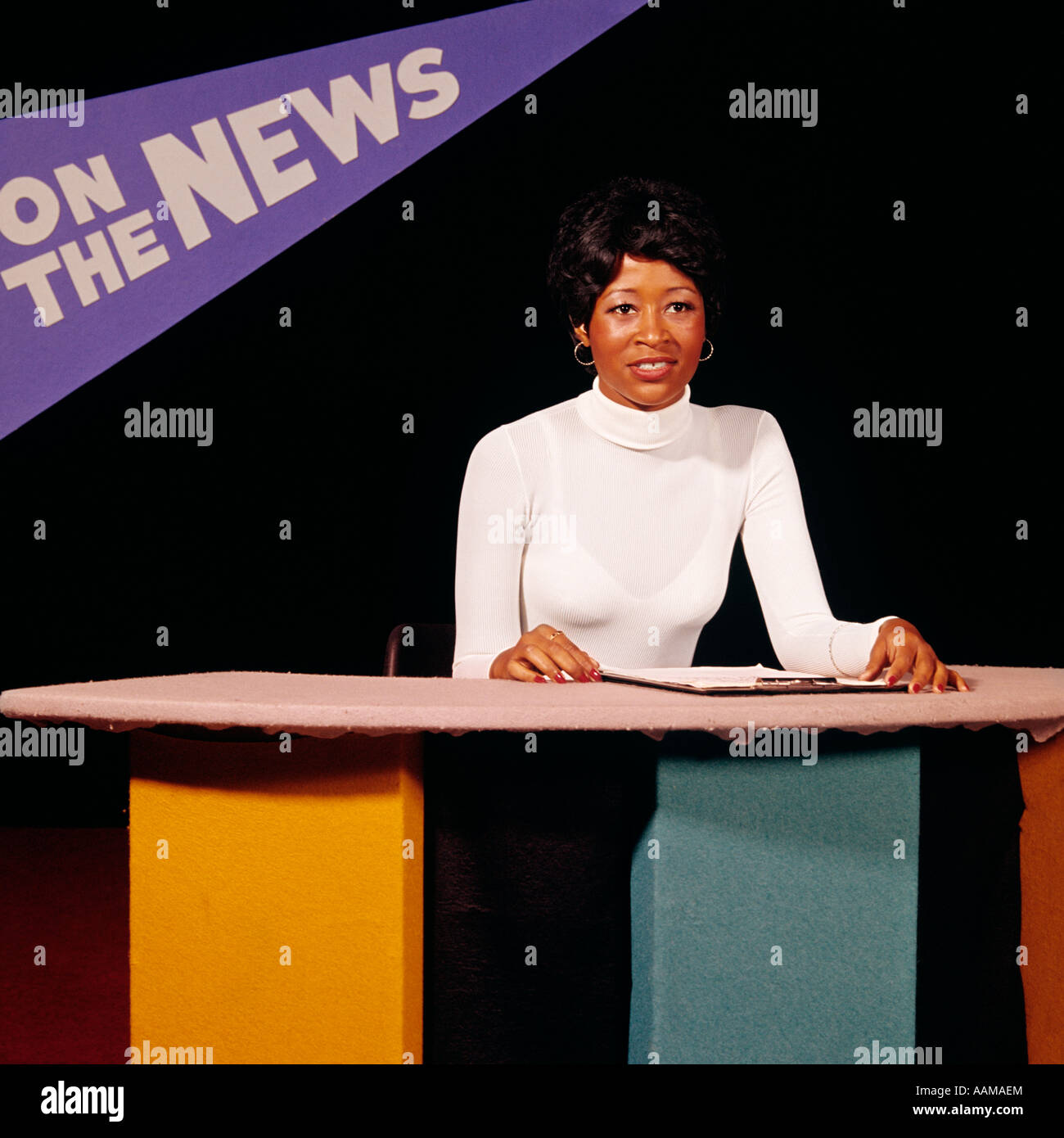 1970s AFRICAN AMERICAN TV ANCHORWOMAN AT BROADCAST DESK WITH STATION ...