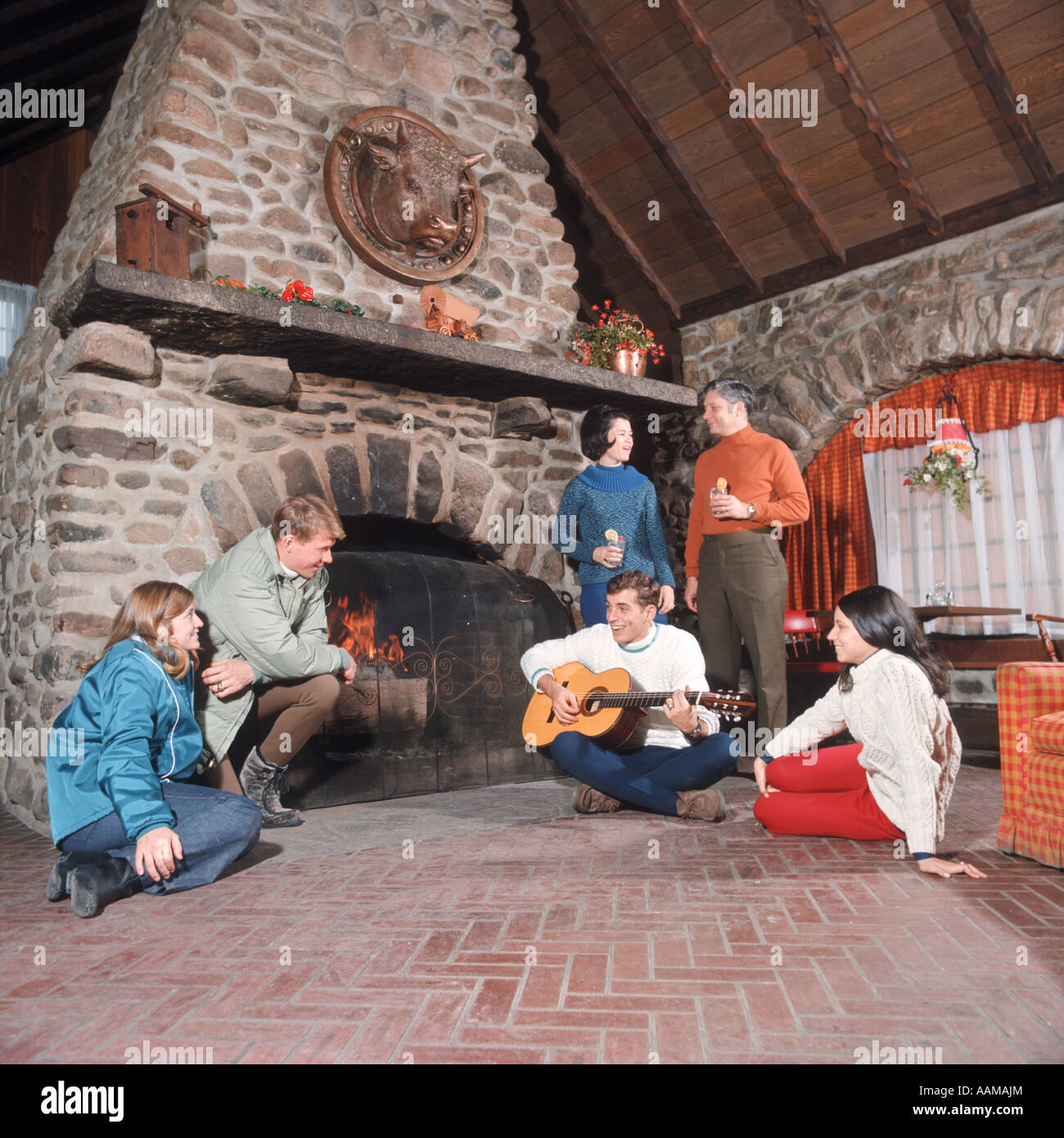 ADULTS INSIDE SKI LODGE SITTING AROUND THE FIRE PLAYING GUITAR Stock ...