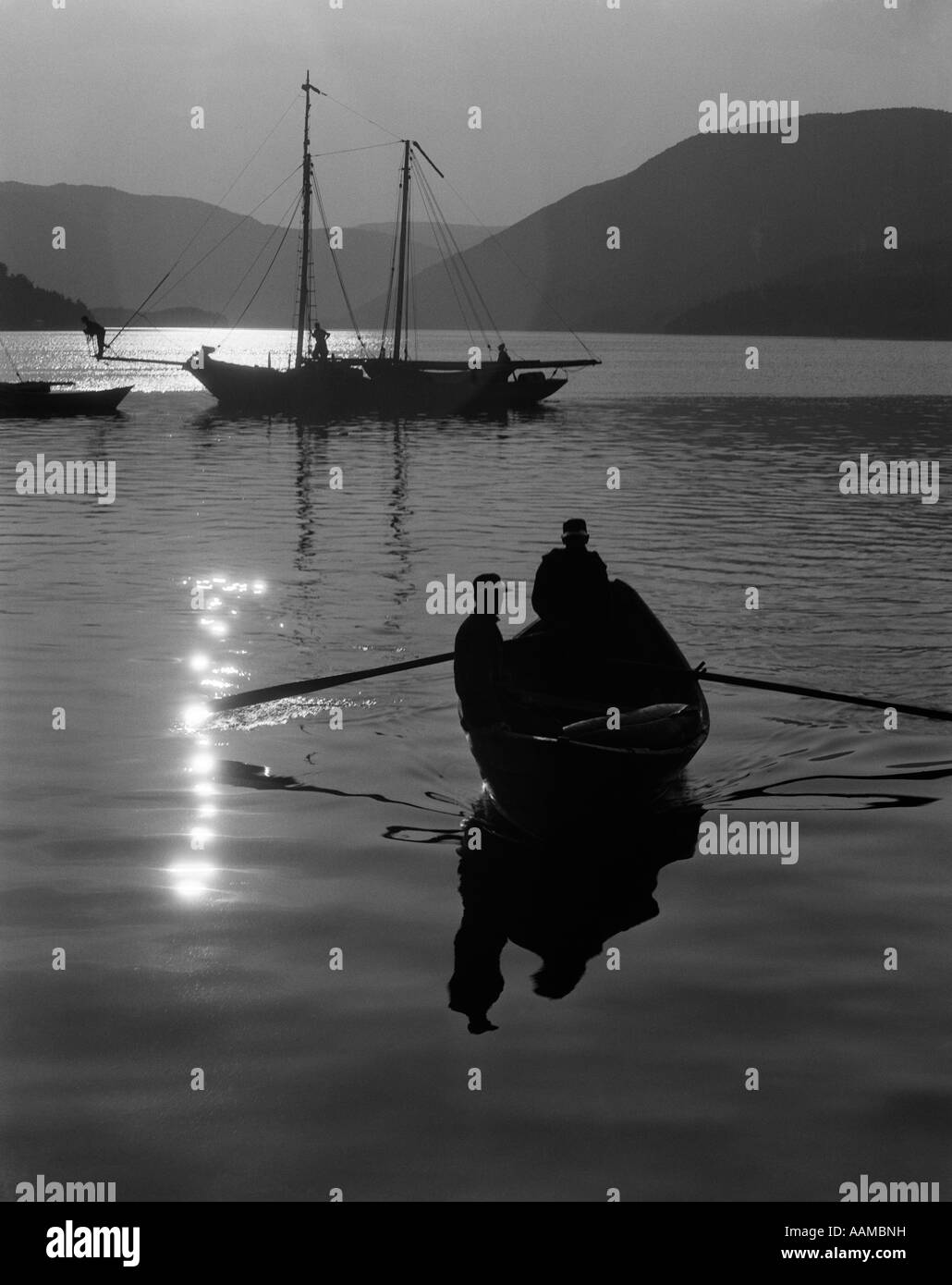 1930s SILHOUETTE OF PAIR OF MEN IN ROWBOAT WITH SAILBOAT IN BACKGROUND ...