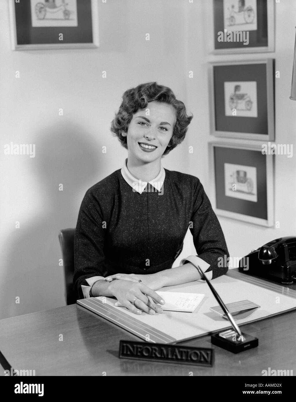 1950s WOMAN SITTING AT INFORMATION DESK IN OFFICE HOLDING PENCIL AND ...