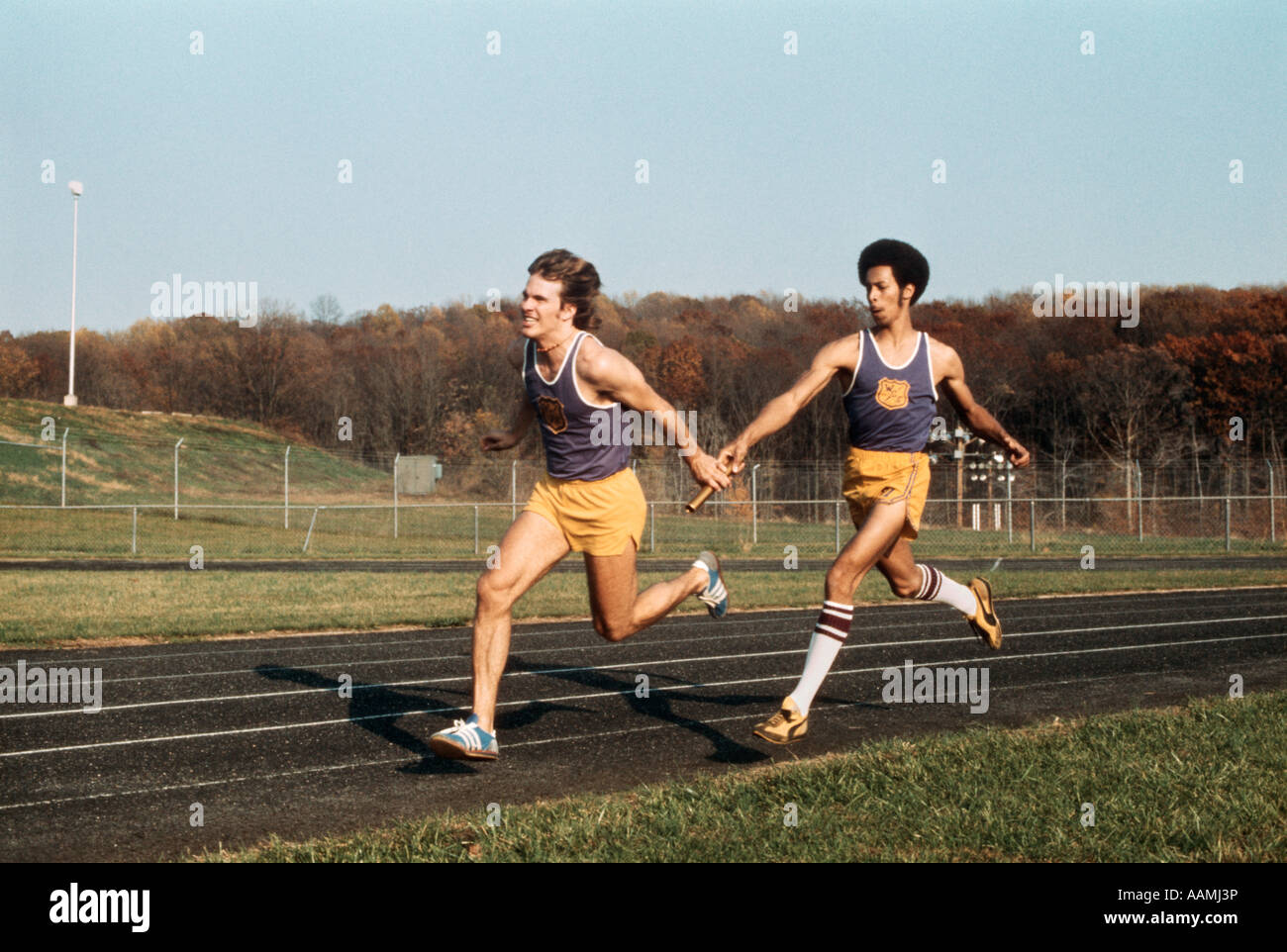 1970s CAUCASIAN AND AFRICAN-AMERICAN MEN PASSING BATON DURING RELAY ...