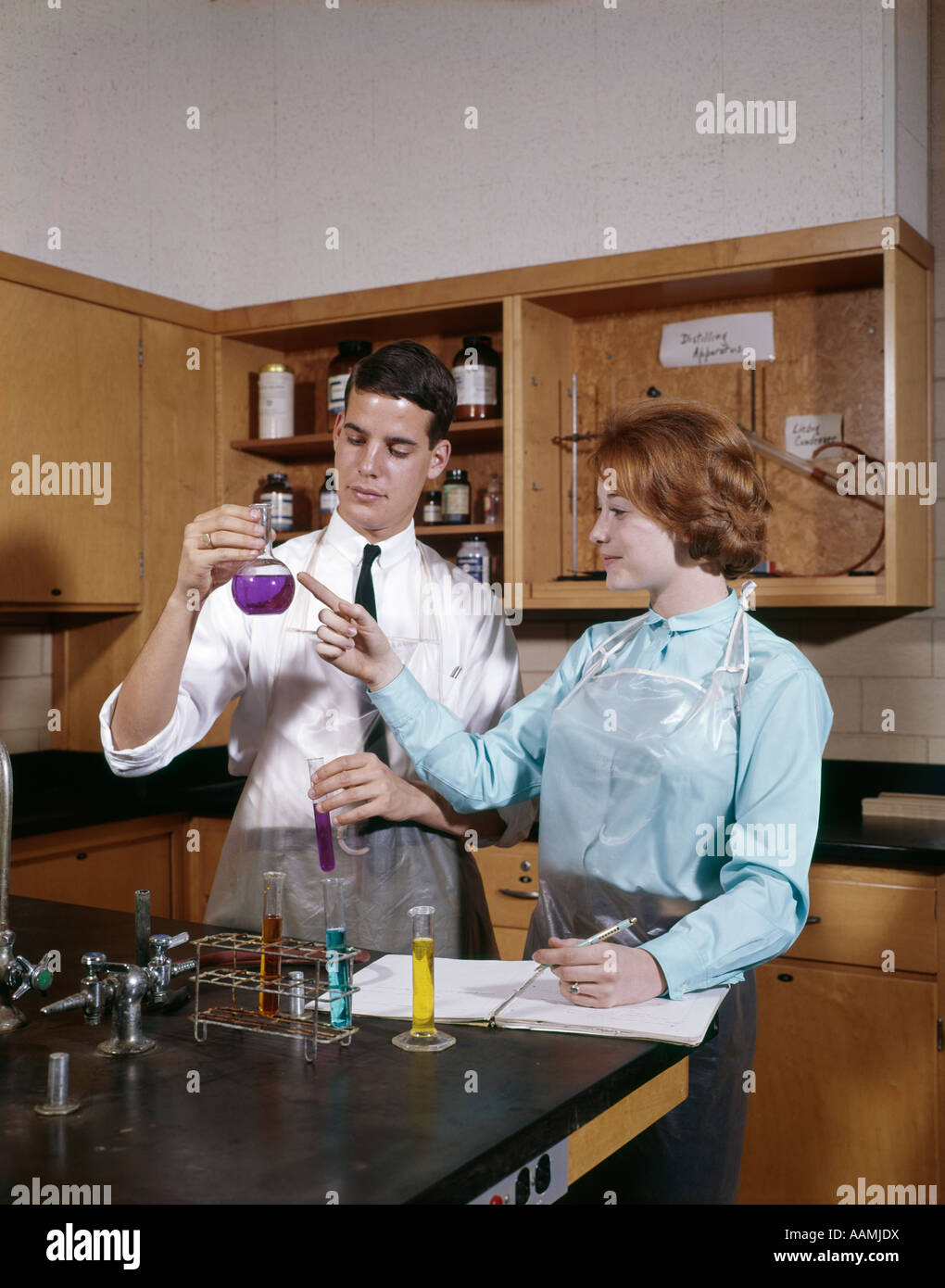 1960s MAN AND WOMAN COLLEGE STUDENTS IN CHEMISTRY LABORATORY LOOKING AT ...