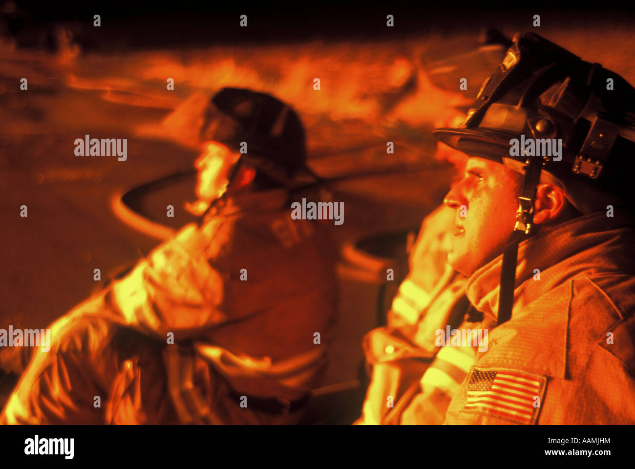 Two fire fighters sitting on a hose putting water on a house on fire ...