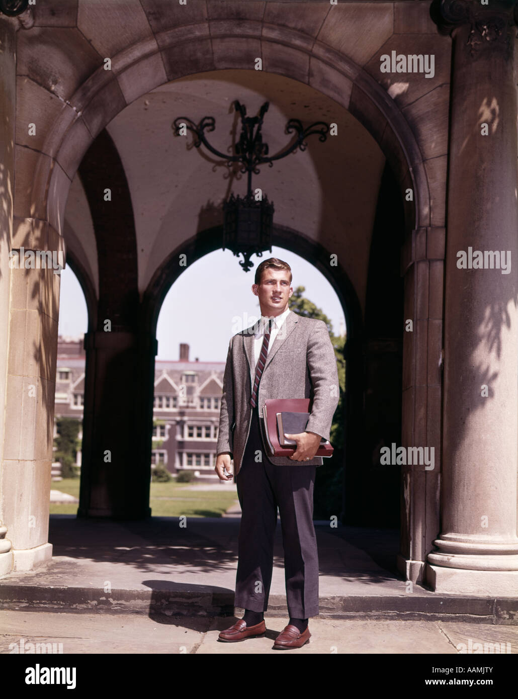 1960s MAN COLLEGE STUDENT STANDING NEAR ARCH LEADING TO COLLEGE CAMPUS ...