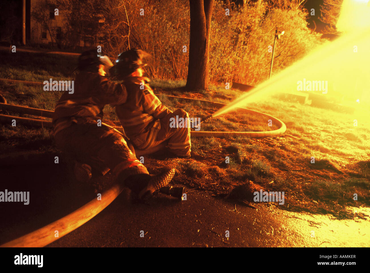 Two fire fighters sitting on a hose putting water on a house Stock ...