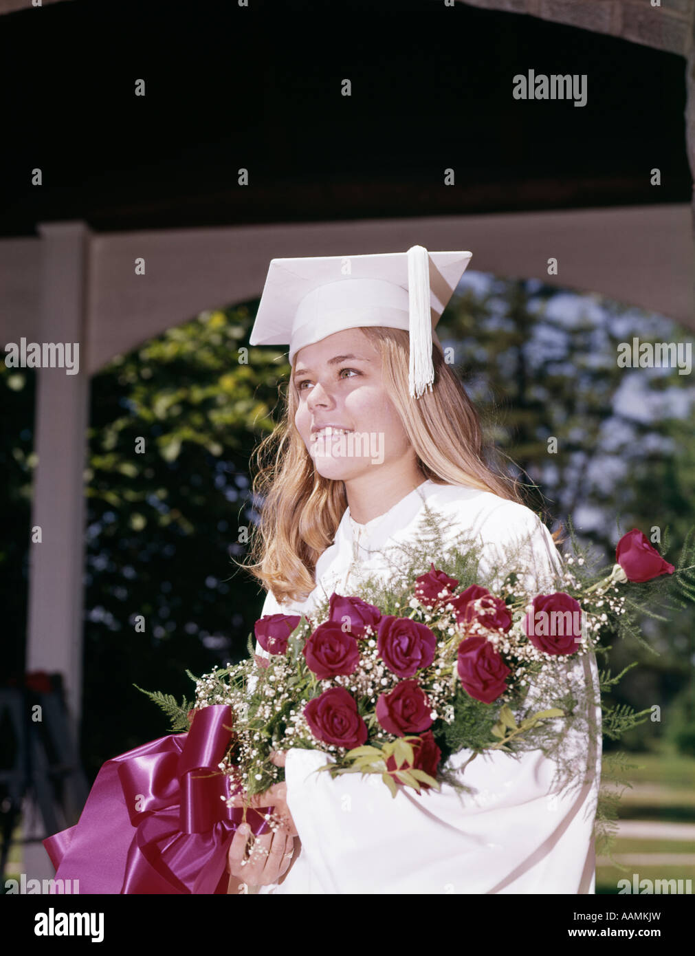 1960s PORTRAIT OF YOUNG WOMAN GRADUATE IN WHITE CAP AND GOWN HOLDING ...
