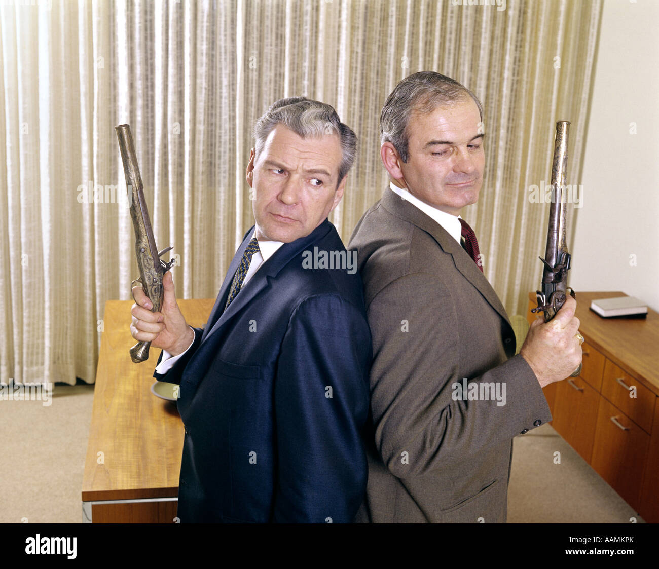 1960s 2 MIDDLE AGED BUSINESS MEN STAND BACK TO BACK HOLDING GUNS ...