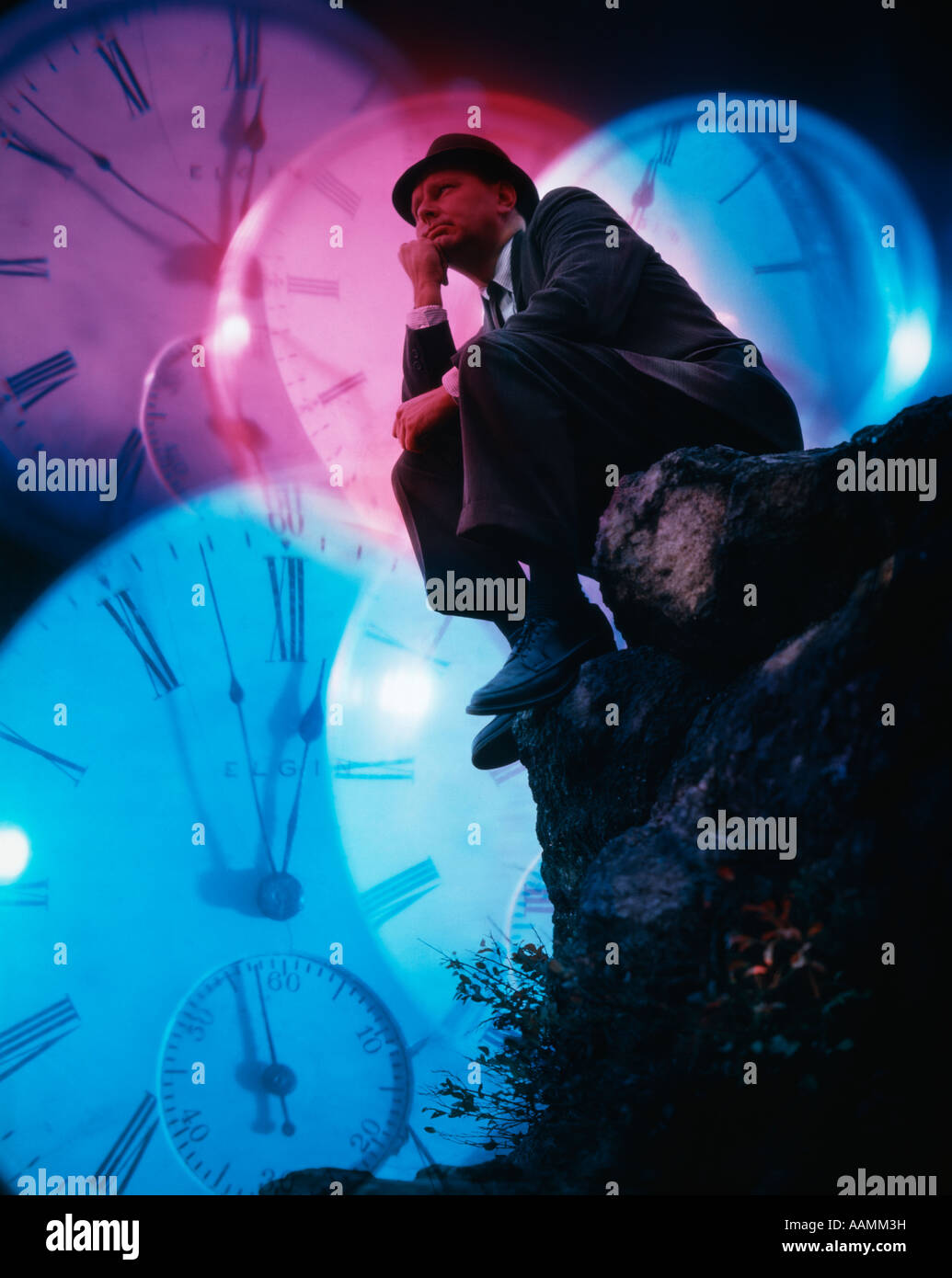 1970s MAN POSED AS THE THINKER ON ROCK WITH HUGE CLOCKS IN BACKGROUND ...