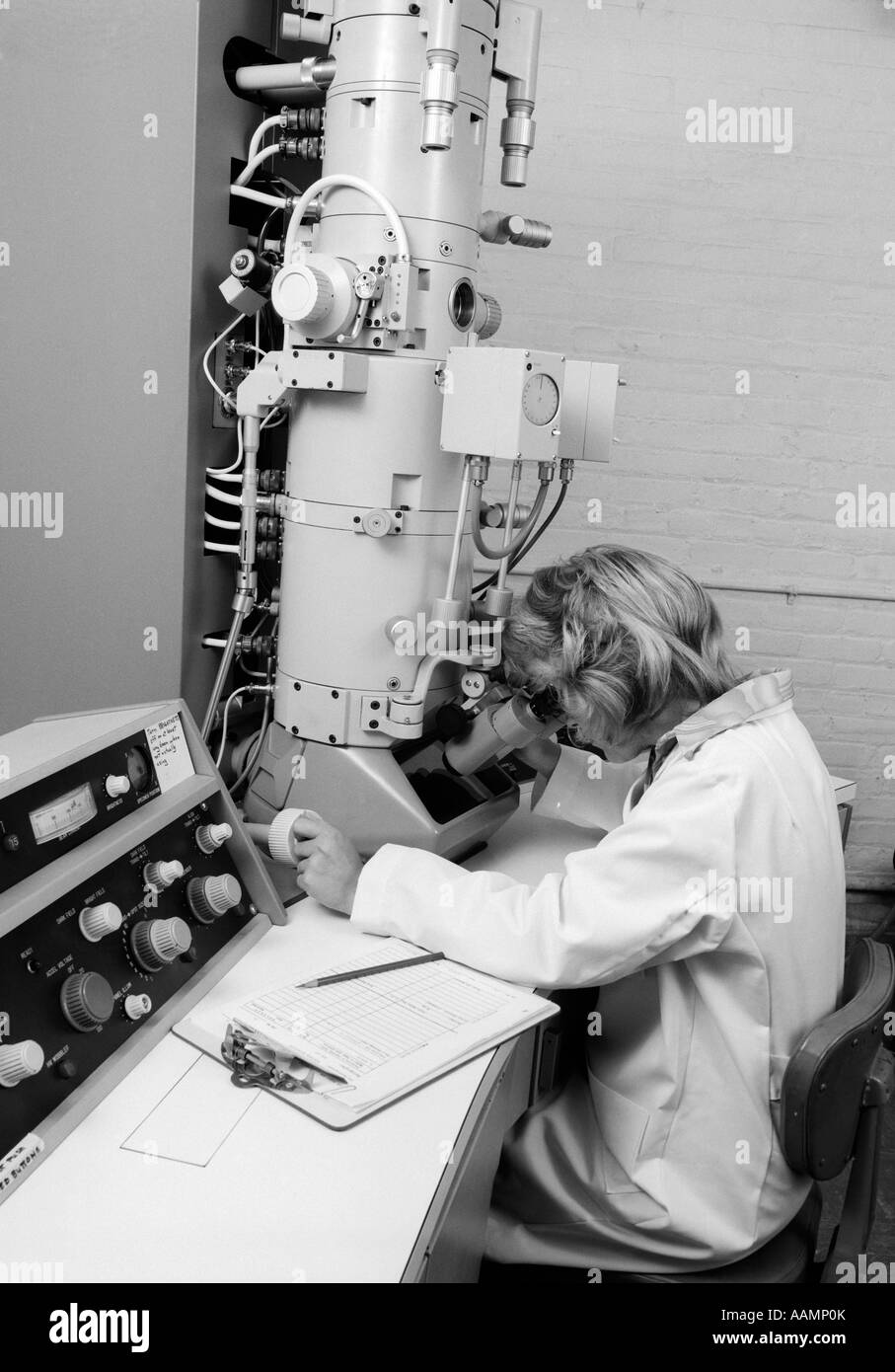 1970s SIDE VIEW OF WOMAN IN LAB COAT LOOKING THROUGH ELECTRON ...