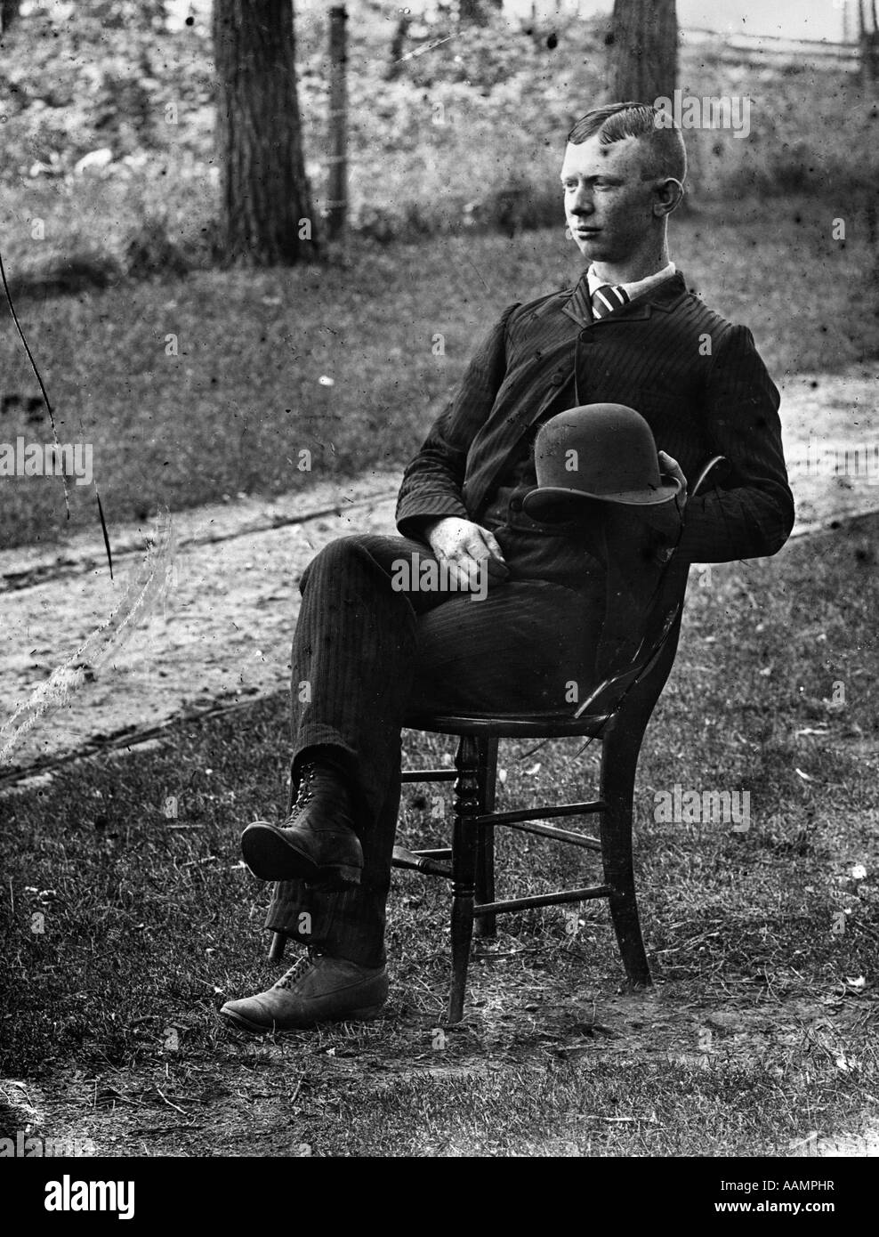 1890s 1900s SIDE VIEW OF MAN WEARING SUIT SEATED ON CHAIR OUTSIDE ...