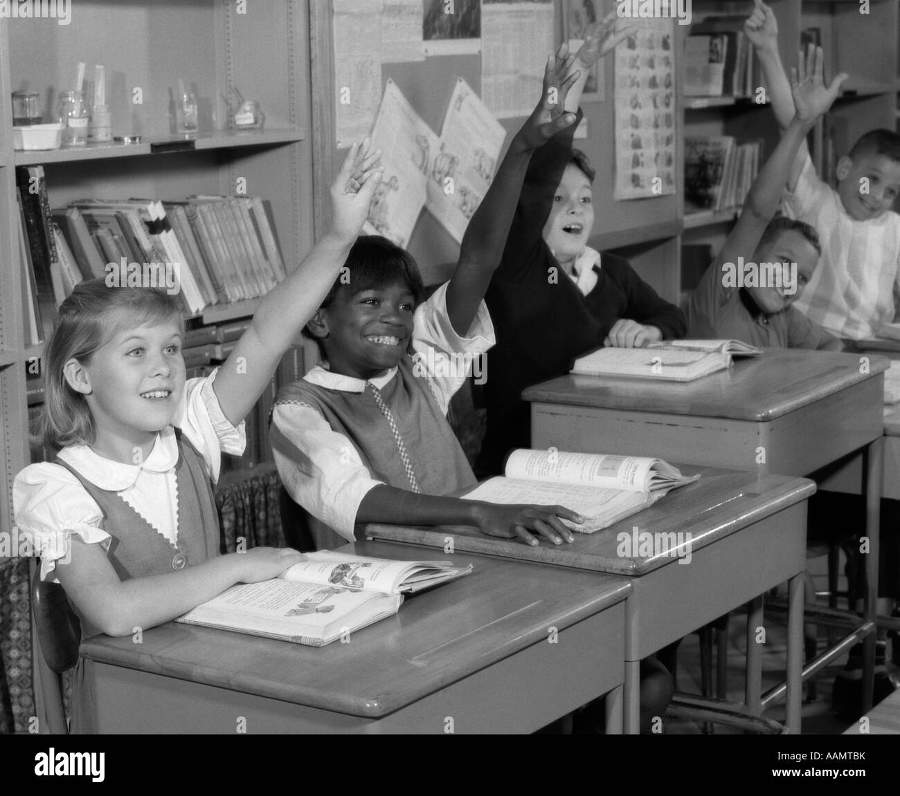 1960s GROUP OF GRADE SCHOOL CHILDREN AT ROW OF DESKS EAGERLY RAISING ...