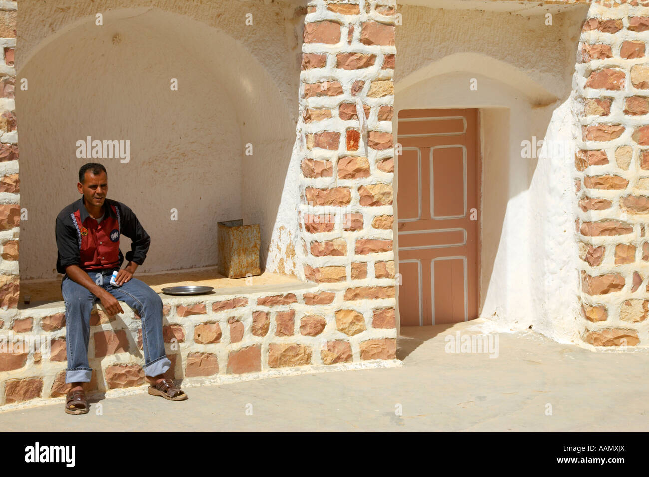 berber troglodyte man sits in the shelter of shade in courtyard of his ...