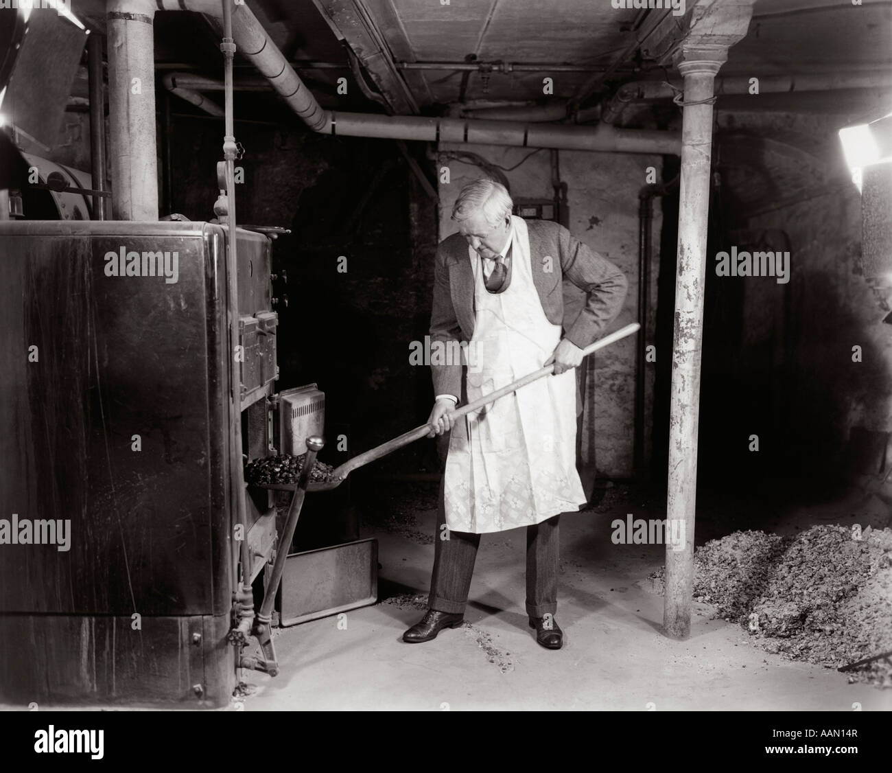 1940s ELDERLY MAN IN BASEMENT WEARING APRON SHOVELING COAL INTO FURNACE ...