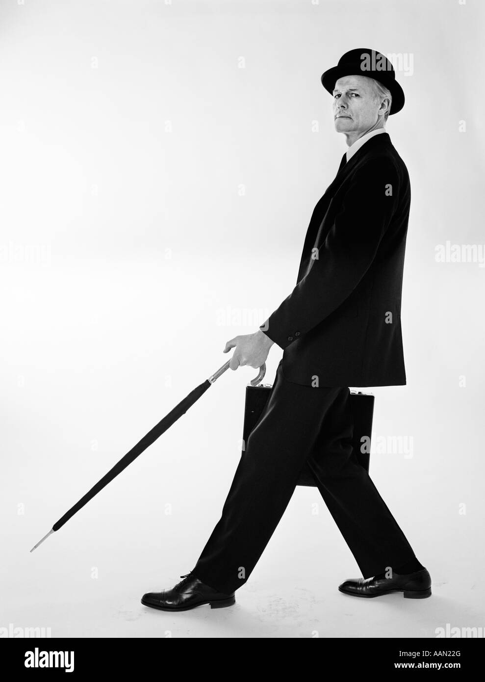 1970s SIDE VIEW OF SALESMAN IN SUIT & BOWLER WITH BRIEFCASE STEPPING ...