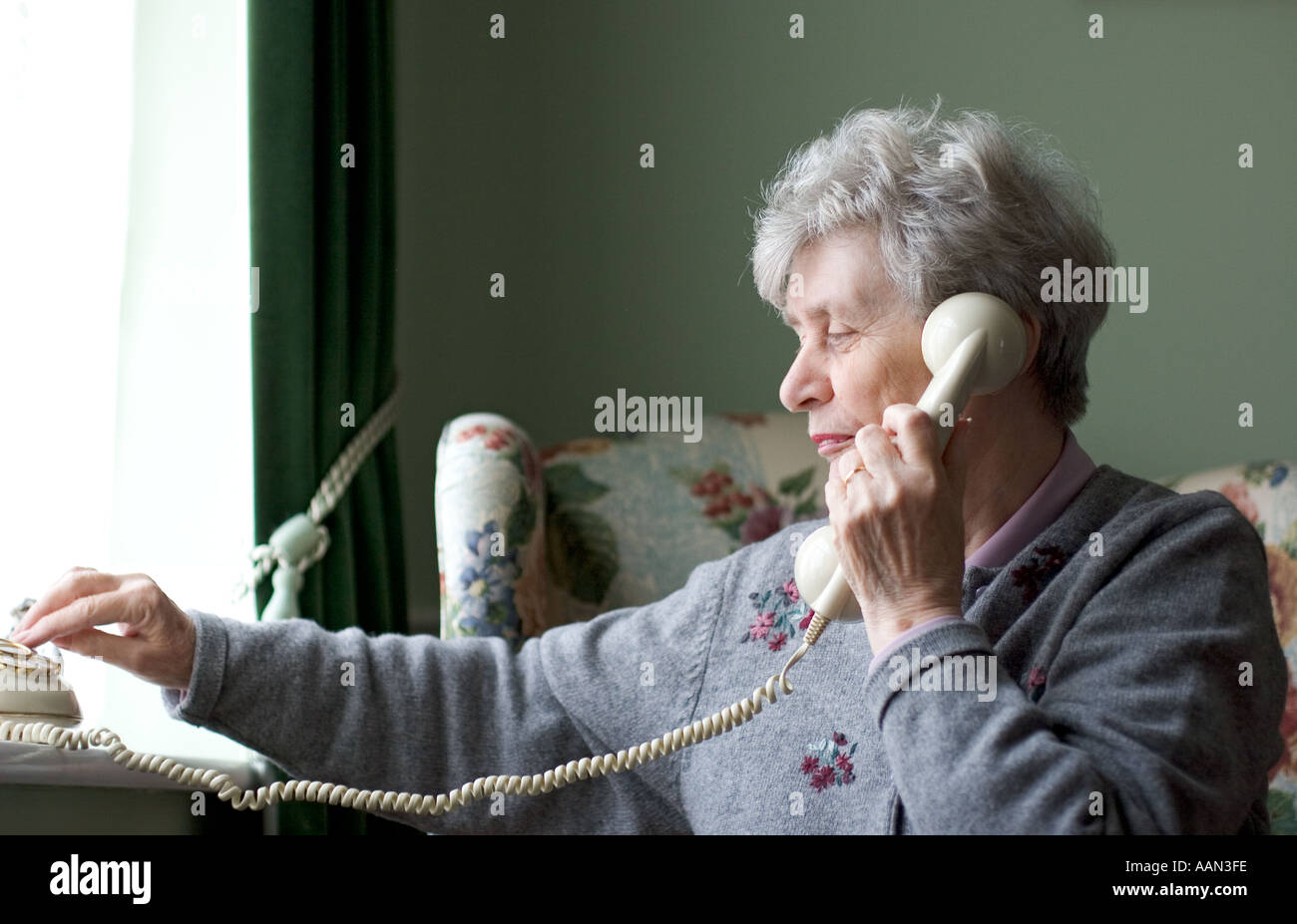Elderly woman using traditional looking telephone in domestic setting ...