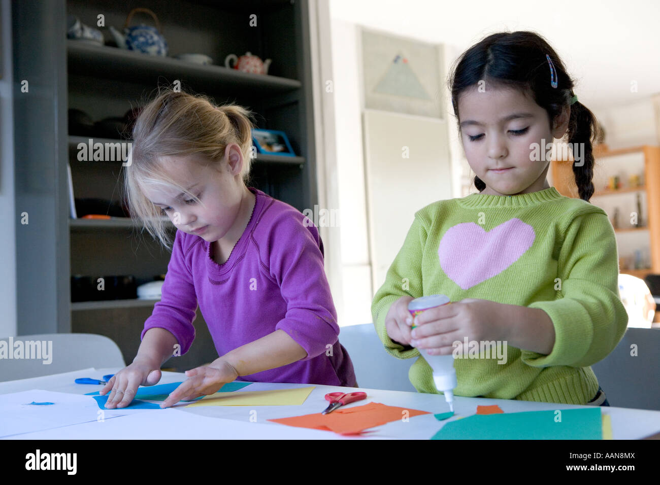 Two little girls are gluing coloured paper Stock Photo - Alamy