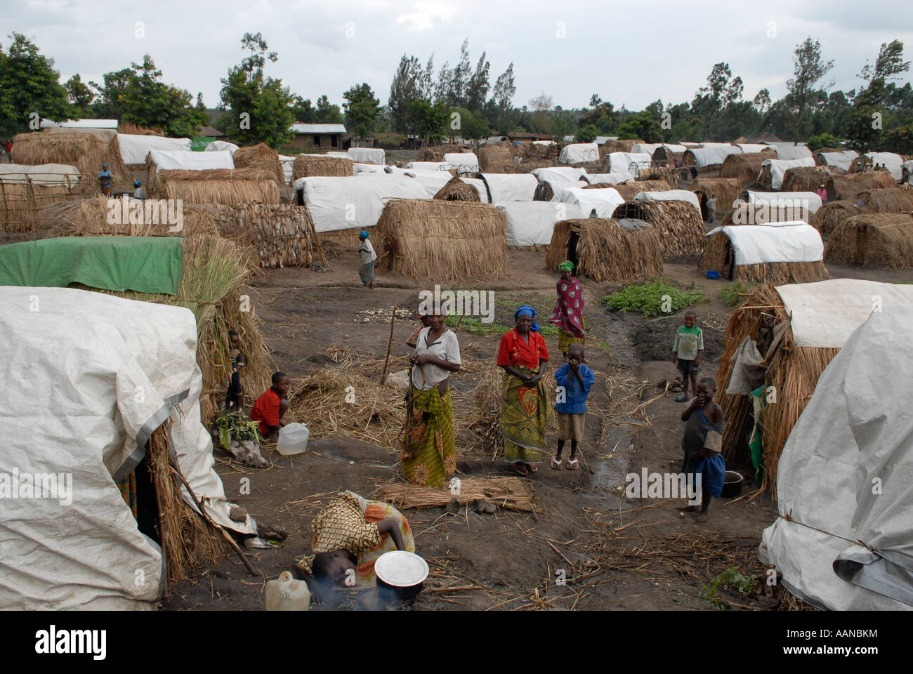 Displaced Congolese people stand amid straw huts covered with plastic ...