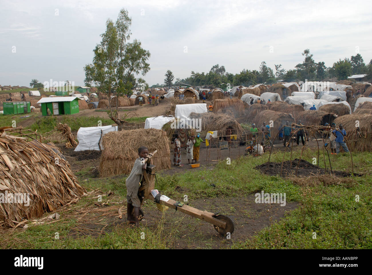 Displaced Congolese people stand amid straw huts covered with plastic ...