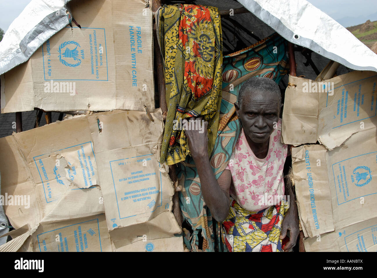 An elderly displaced Congolese woman peers out of a makeshift straw hut ...