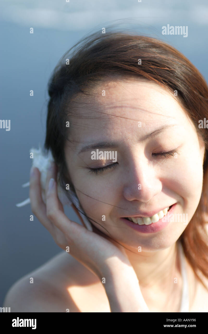 A young woman listening a shell Stock Photo - Alamy